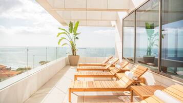 Terraço no telhado com cadeiras de lounge de madeira, plantas em vasos e vista para o oceano.