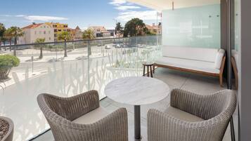 Uma varanda com mobiliário de vime, uma mesa de mármore e vista para a rua e edifícios.