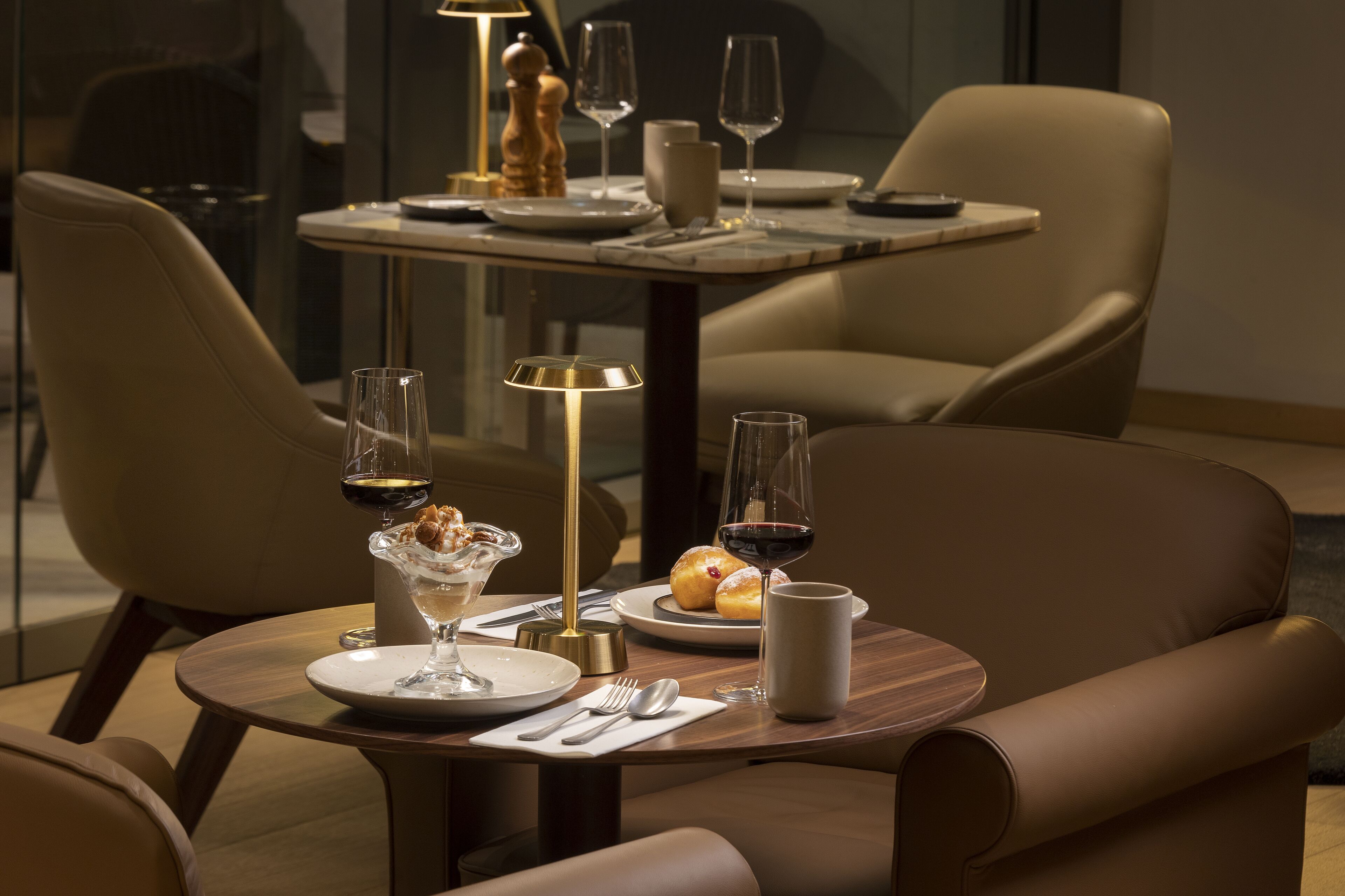 Uma área de refeições com uma mesa posta para dois, incluindo uma vela, taças de vinho e um prato de doces.