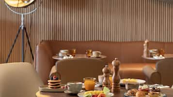 Uma sala de jantar com mesa posta para o café da manhã, incluindo pratos de comida, xícaras e um abajur.