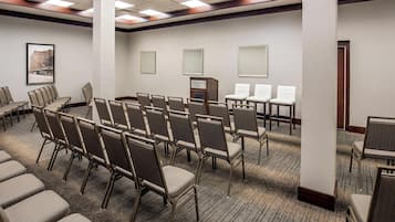 Uma sala de conferências com fileiras de cadeiras, um pódio e quadros nas paredes.