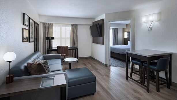 Quarto de hotel moderno com sofá, pequena mesa de jantar, escrivaninha, televisão e cama.