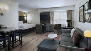 Quarto de hotel com cama, escrivaninha, sofá e uma mesinha.