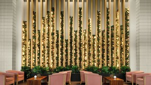 Decoração moderna com ripas de madeira verticais adornadas com plantas e luzes, assentos cor-de-rosa e uma mesa de centro de madeira.