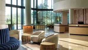 Um hall amplo com balcão de atendimento, área de estar e grandes janelas com vista para o verde.