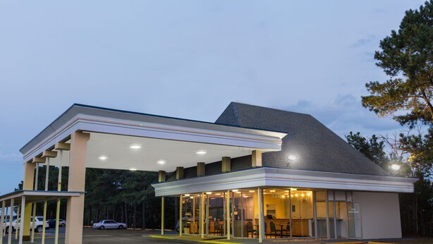 Um posto de gasolina com área coberta e um edifício com telhado inclinado.