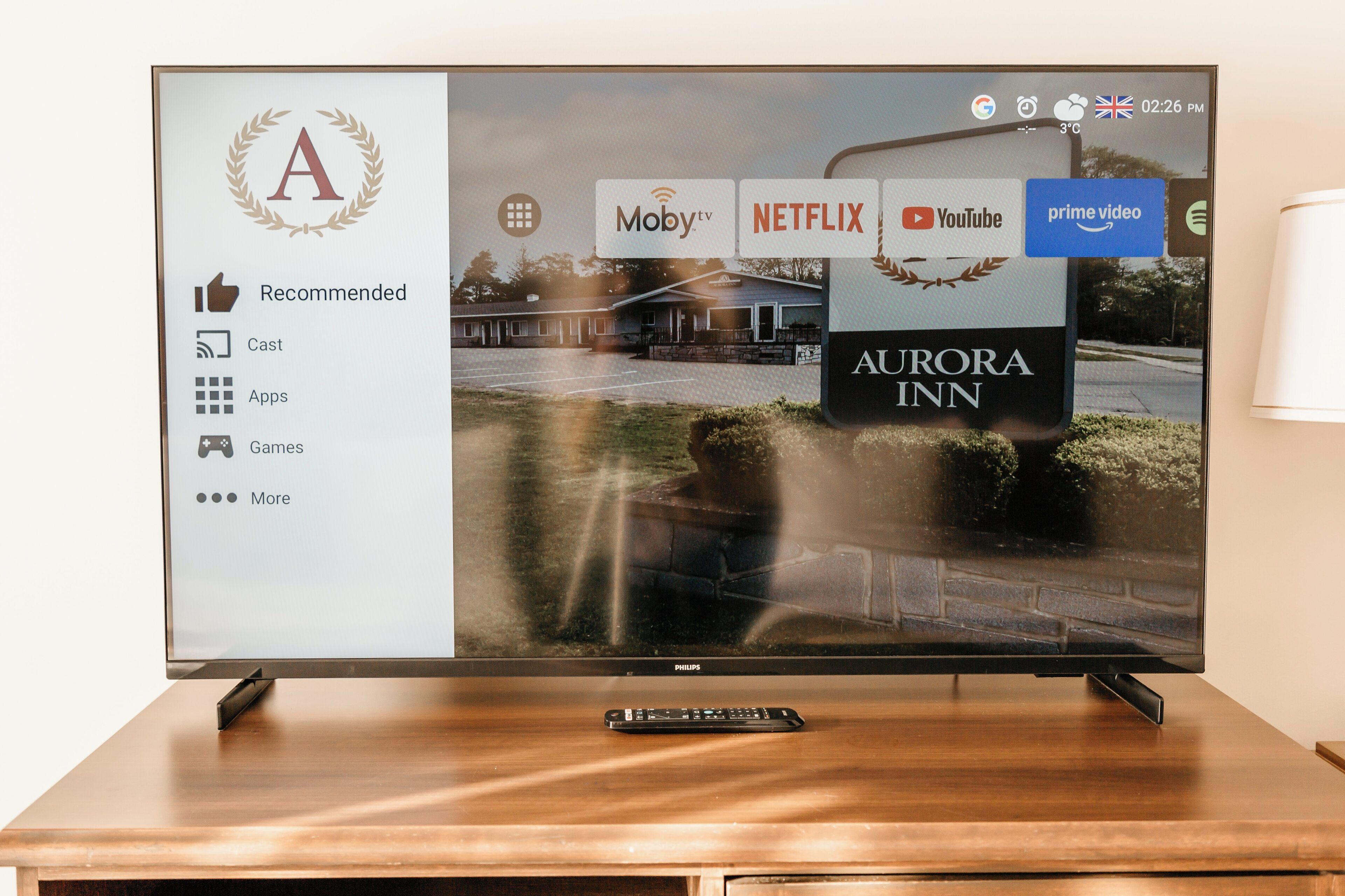 Uma televisão mostrando um letreiro de hotel da Aurora Inn, com um controle remoto sobre um suporte de madeira.