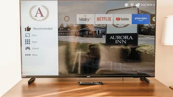 Uma televisão mostrando um letreiro de hotel da Aurora Inn, com um controle remoto sobre um suporte de madeira.