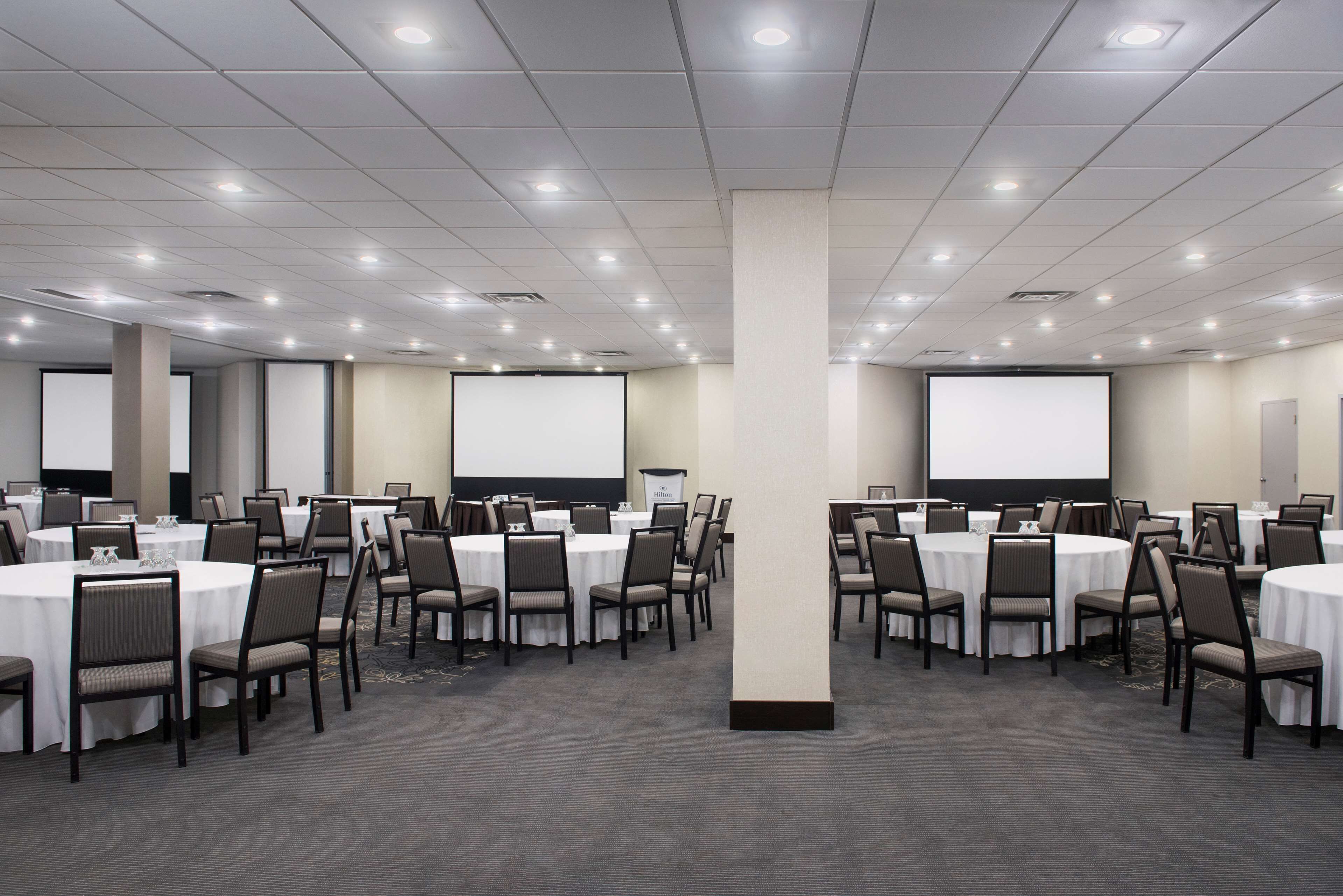 Uma sala de conferências com várias mesas redondas e cadeiras, equipada com projetores e telas.