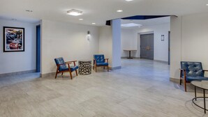 Um hall amplo com design moderno, com área de estar com cadeiras azuis, uma mesa redonda e um quadro na parede.