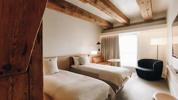 Quarto de hotel com duas camas, um sofá, uma cadeira e uma mesinha.