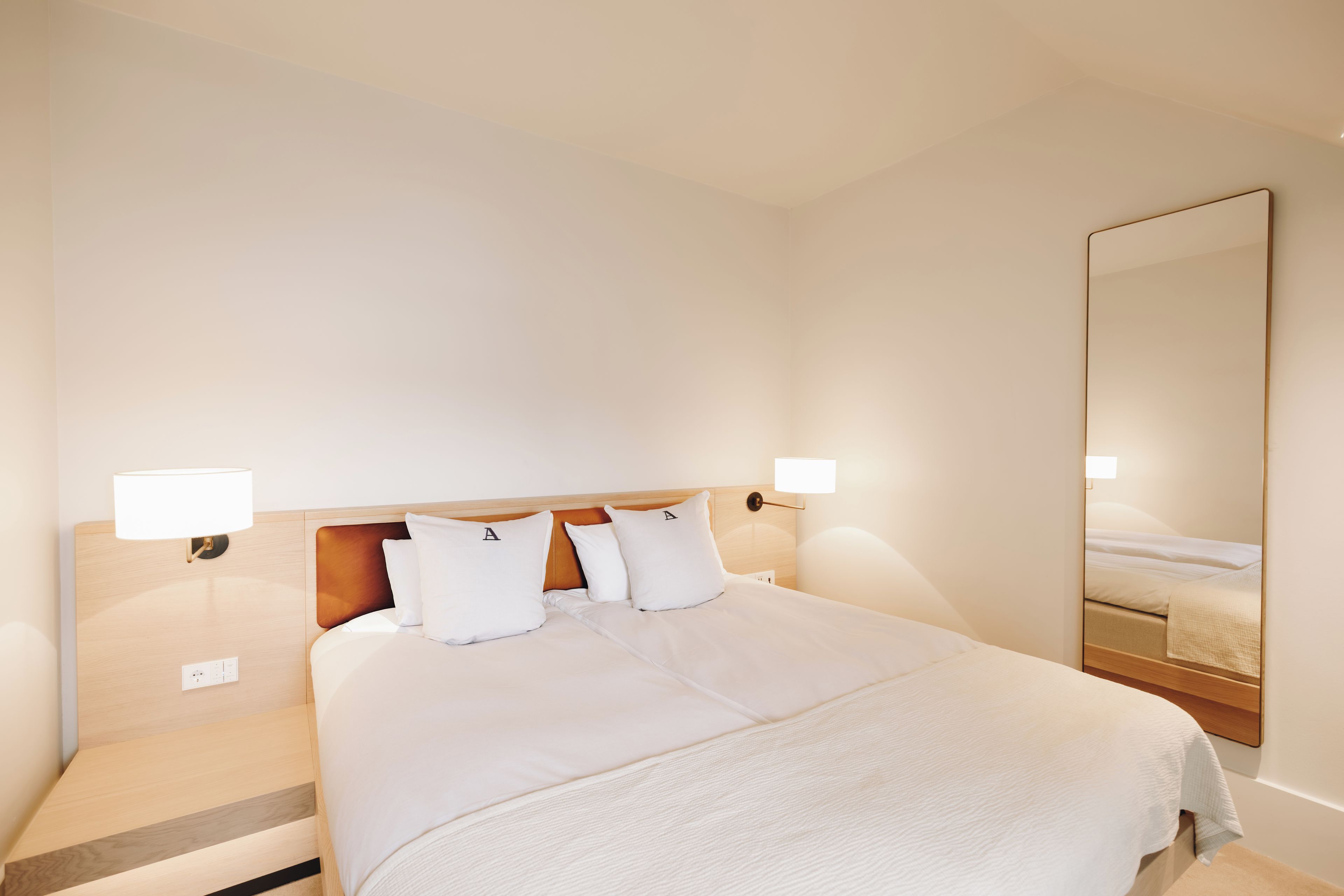 Quarto de hotel com uma cama grande, duas luminárias de cabeceira, mesa de cabeceira e espelho.