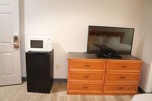 Quarto de hotel compacto com micro-ondas, televisão de tela plana em penteadeira de madeira e porta com fechadura.