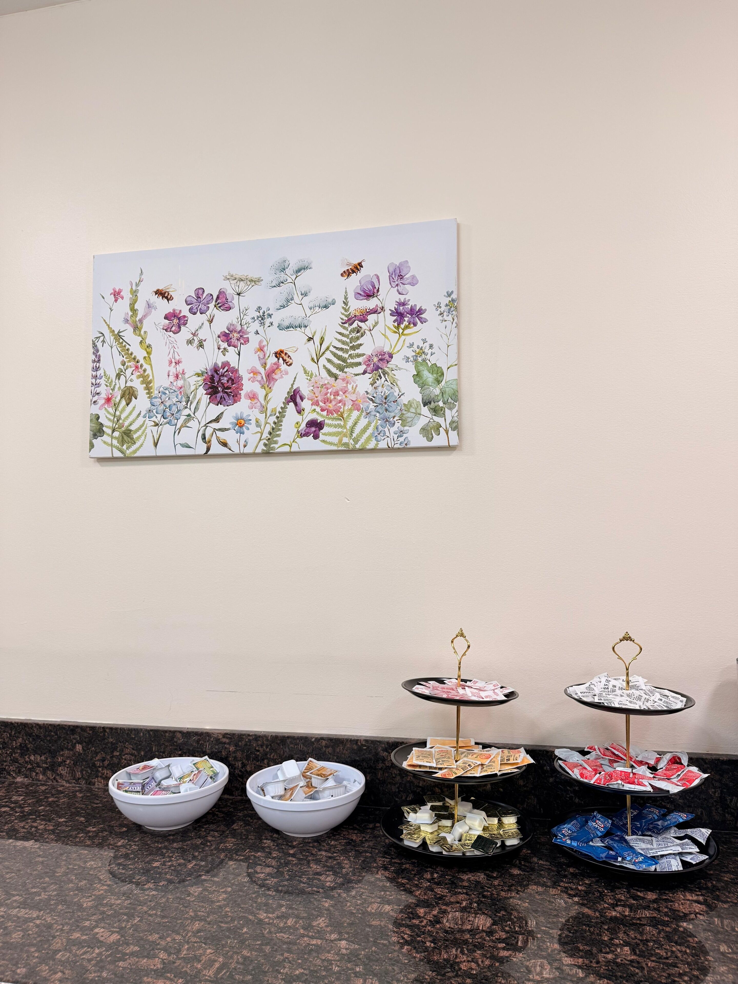 Paredes com pintura floral e três suportes escalonados para sobremesas em bancada de mármore.