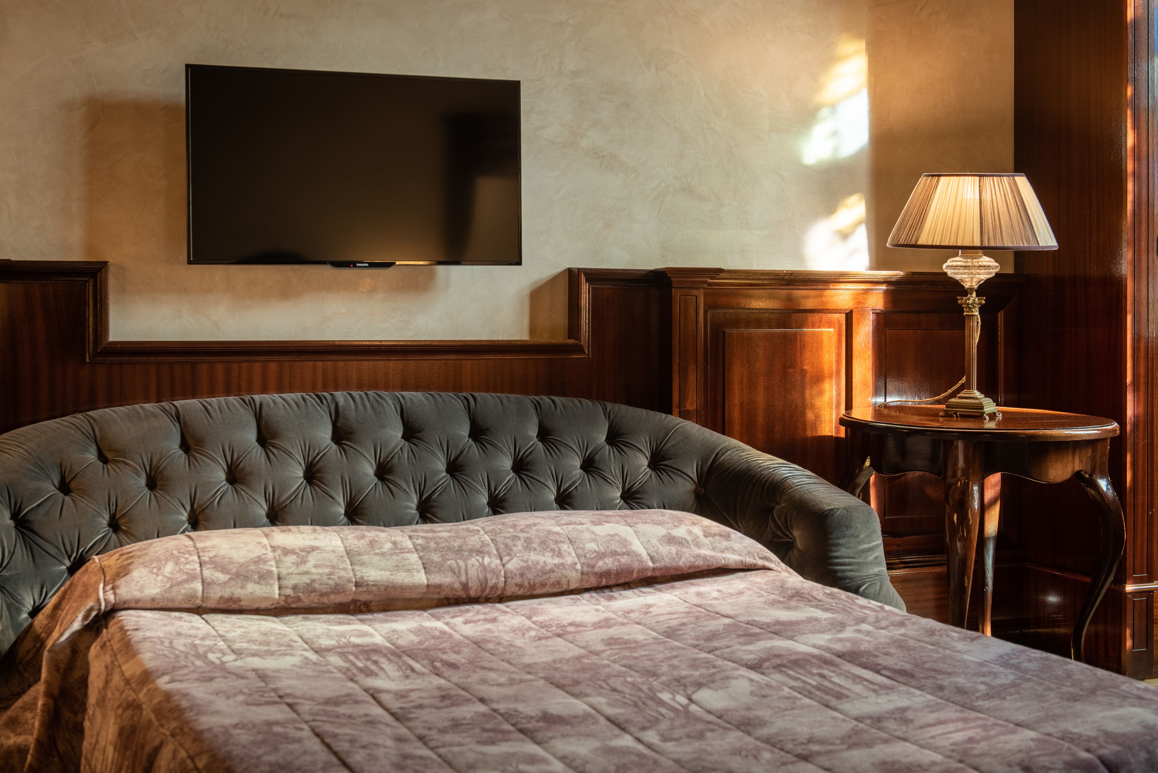 Quarto com uma cama grande, televisão de tela plana na parede e uma mesa com abajur.