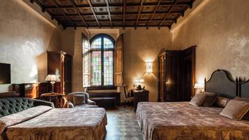 Quarto com duas camas, uma grande janela em arco, teto de madeira e televisão na parede esquerda.