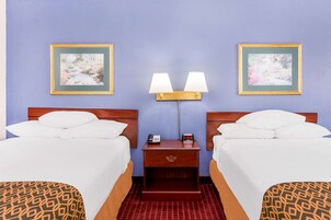 Quarto de hotel com duas camas, uma mesa de cabeceira com abajur e duas fotos emolduradas na parede.