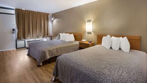 Quarto de hotel com duas camas, uma mesa de cabeceira com abajur, telefone e janela com cortinas.
