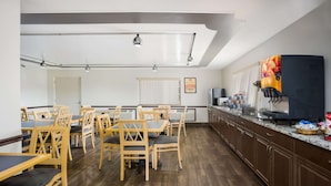 Uma área de refeições com cadeiras e mesas de madeira, uma máquina de café e um balcão com diversos objetos.
