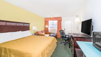 Quarto de hotel com cama, escrivaninha, cadeira, televisão e janela com cortinas.