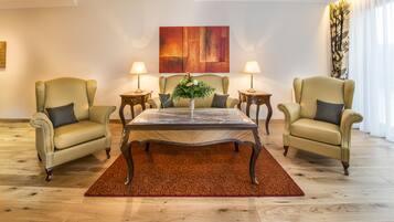 Uma sala de estar bem iluminada com uma mesa de centro, duas poltronas, um sofá e um quadro decorativo na parede.