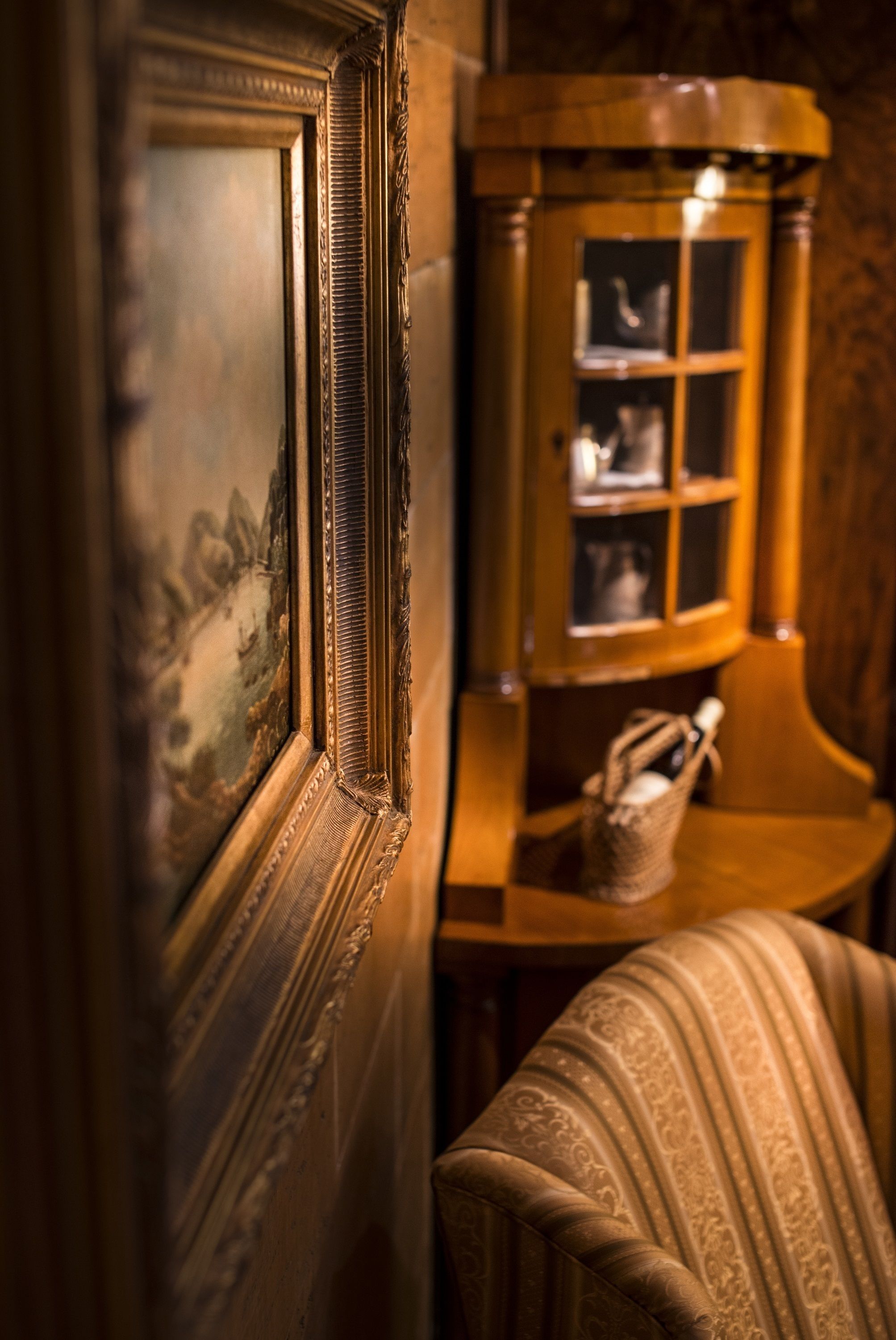 Um quarto com um armário de madeira com portas de vidro, uma obra de arte emoldurada na parede e uma cadeira estampada.