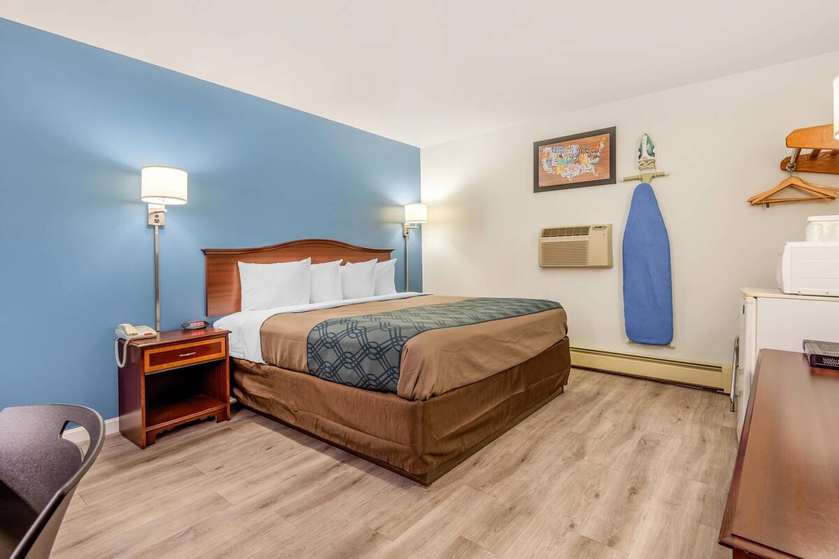 Quarto de hotel com cama, abajures, escrivaninha, cadeira e cômoda.
