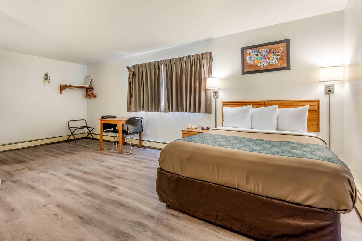Quarto de hotel com uma cama grande, uma mesa com cadeira, um telefone e um mapa na parede.