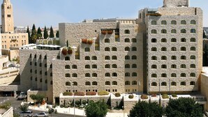 Um edifício grande, de vários andares, com fachada de pedra, várias janelas e varandas com plantas em vasos.