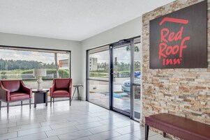 Um saguão de hotel com a placa Red Roof Inn, poltronas de couro, uma mesinha e vista para o estacionamento.