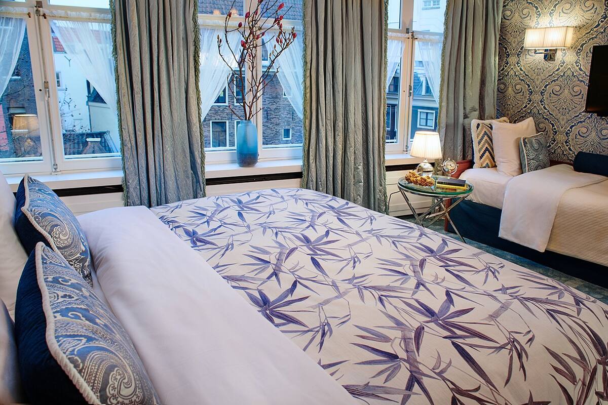 Quarto de hotel com cama grande, mesa de cabeceira, abajur e vista para edifícios.
