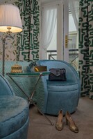 Quarto com uma poltrona azul, uma mesinha com abajur, uma bolsa e um par de sapatos.