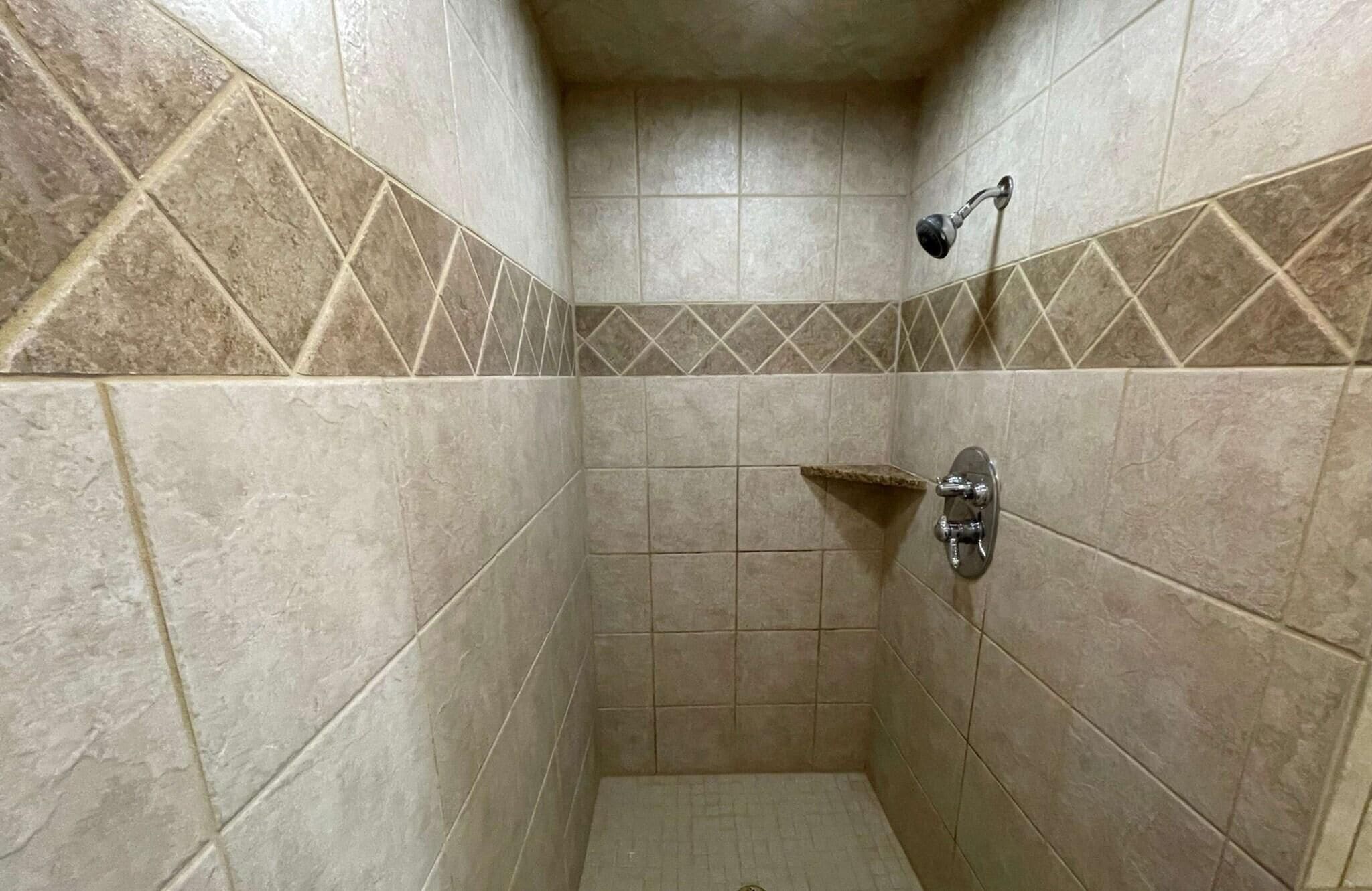 Pequeno espaço de chuveiro com azulejos, chuveiro manual e torneira fixada na parede.