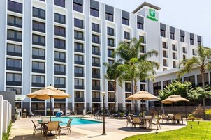 Um hotel com área de piscina, mobiliário de exterior e palmeiras.