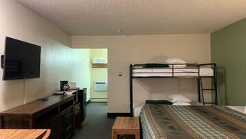 Quarto de hotel com beliches, uma escrivaninha com computador, televisão e uma mesinha.