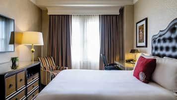 Quarto de hotel com uma cama grande, uma escrivaninha com luminária, uma cadeira e um armário.