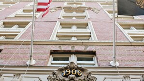Fachada de edifício com um letreiro grande com o número '1900', janelas amplas e um mastro com uma bandeira.
