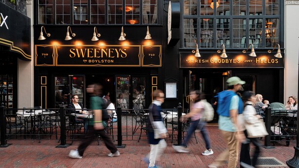 Um restaurante chamado "SWEENEYS ON BOYLTON", com mesas ao ar livre e fachada preta.