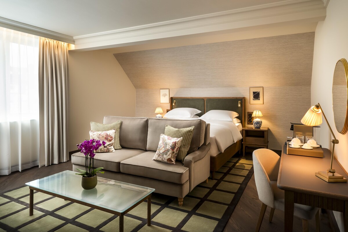 Quarto de hotel com cama, sofá, mesa de centro e escrivaninha.