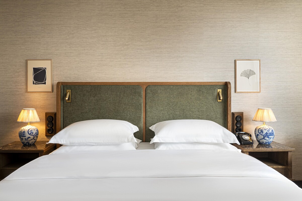 Quarto de hotel com cama de casal, duas mesas de cabeceira com abajures e quadros decorativos nas paredes.
