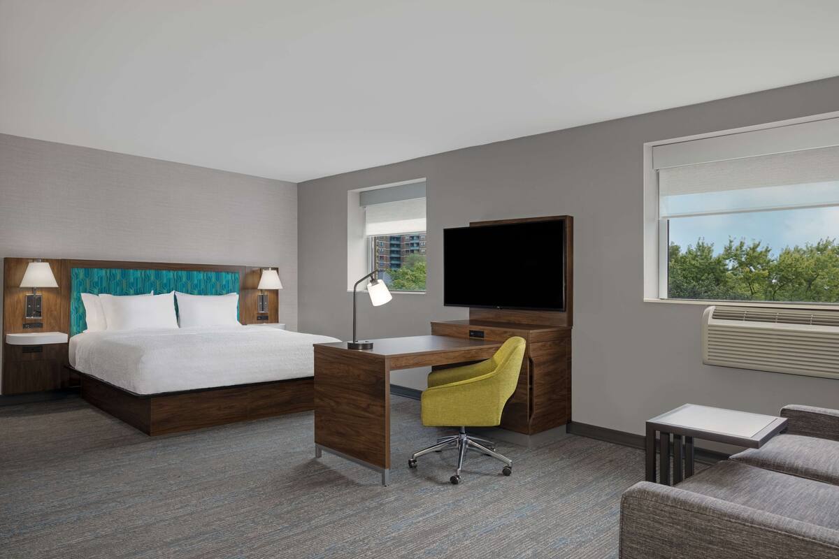 Quarto de hotel com cama, escrivaninha, cadeira, televisão e janela com vista.