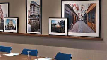 Uma sala de conferências com uma mesa redonda, cadeiras azuis, quadros nas paredes e uma luminária no teto.