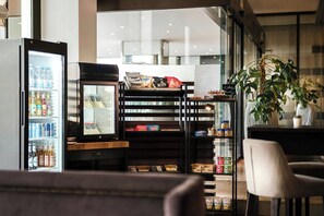 Um saguão de hotel com um refrigerador cheio de bebidas, uma máquina de vendas automática e um quadro de menu.