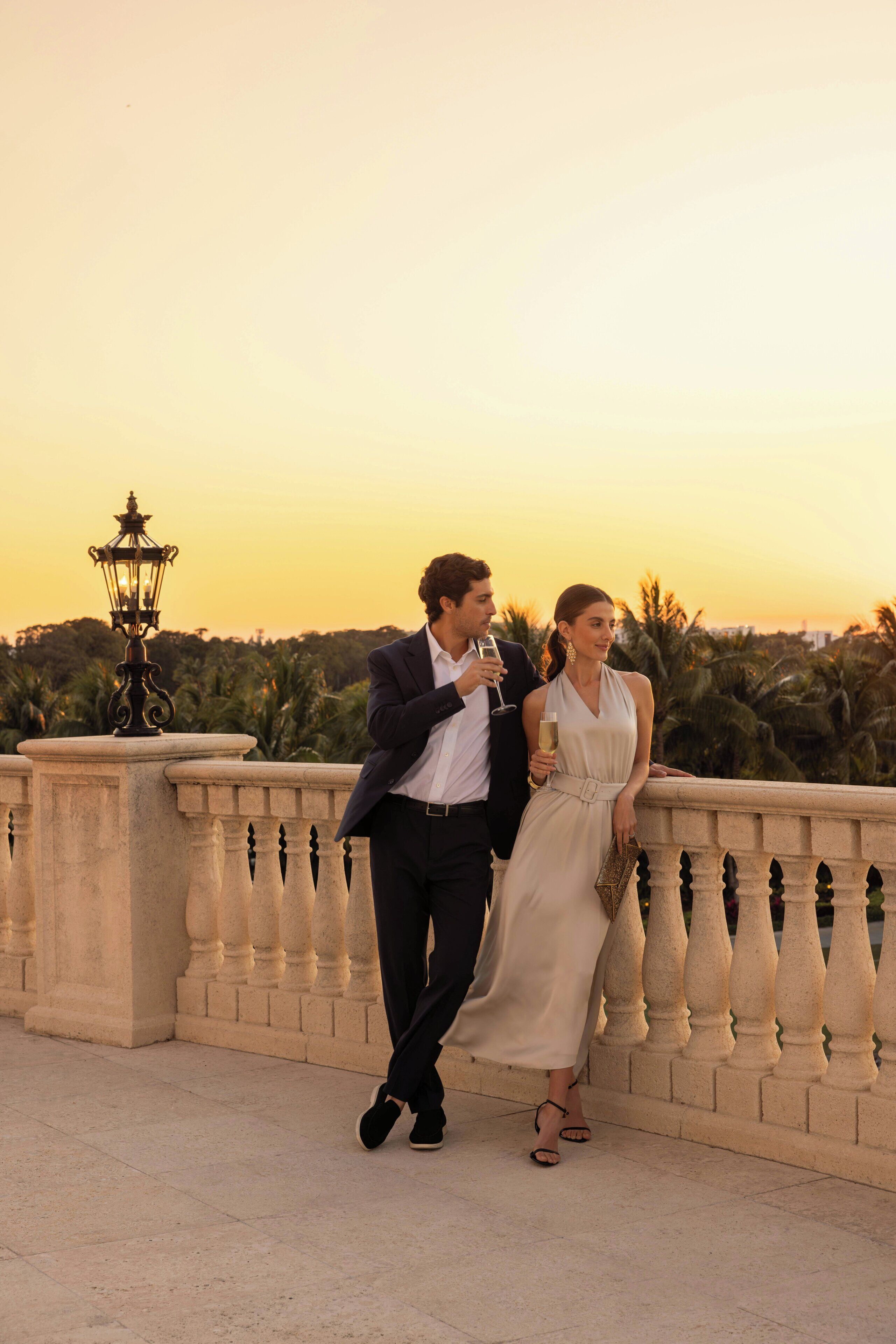 Um casal em uma varanda com vista para o pôr do sol, um poste de luz e um corrimão.