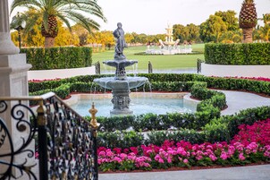 Um jardim paisagístico com uma fonte central, sebes bem aparadas e uma estátua.