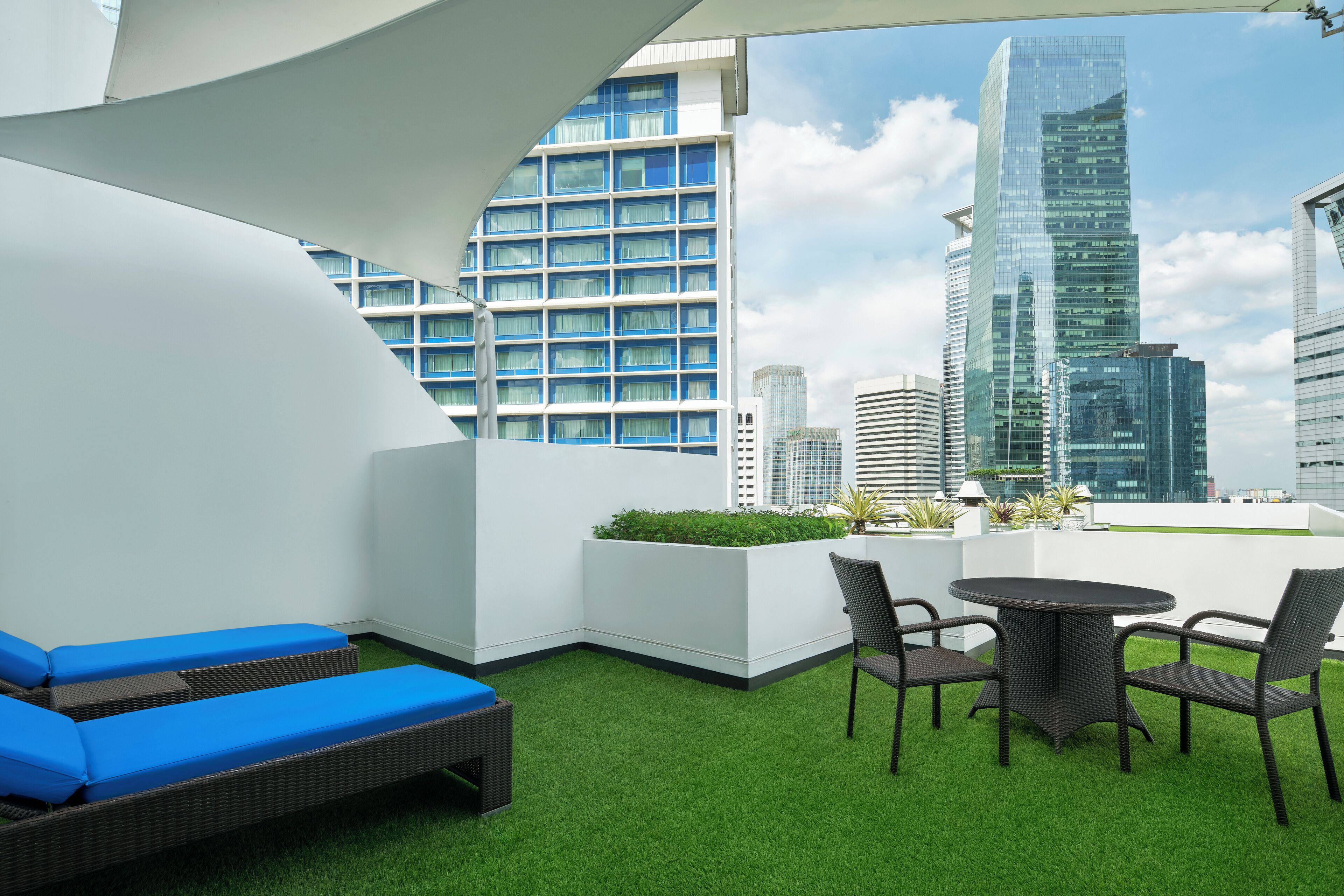Terraço no terraço com grama sintética, área de estar com almofadas azuis e uma mesa com cadeiras.
