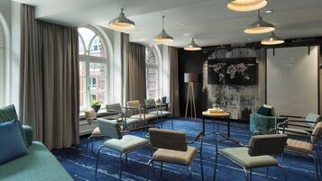 Quarto de hotel com carpete azul, vários espaços de estar e janelas amplas com cortinas.