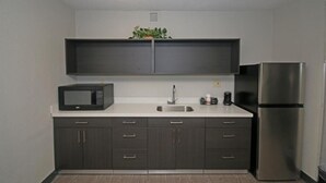 Uma cozinha moderna com armários escuros, uma geladeira de aço inoxidável, micro-ondas e pia.