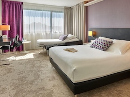 Quarto de hotel com duas camas, uma escrivaninha, uma cadeira e uma mesa pequena.