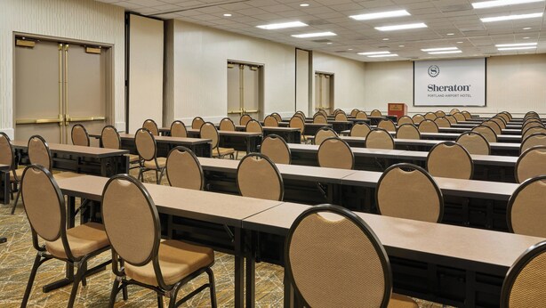 Salão de conferências do Sheraton Portland Airport Hotel, com mesas e cadeiras dispostas em fileiras, uma tela grande e piso coberto de carpete.